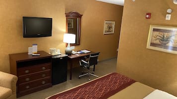 Quarto de hotel com cama, escrivaninha com luminária, televisão, cômoda e uma cadeira.