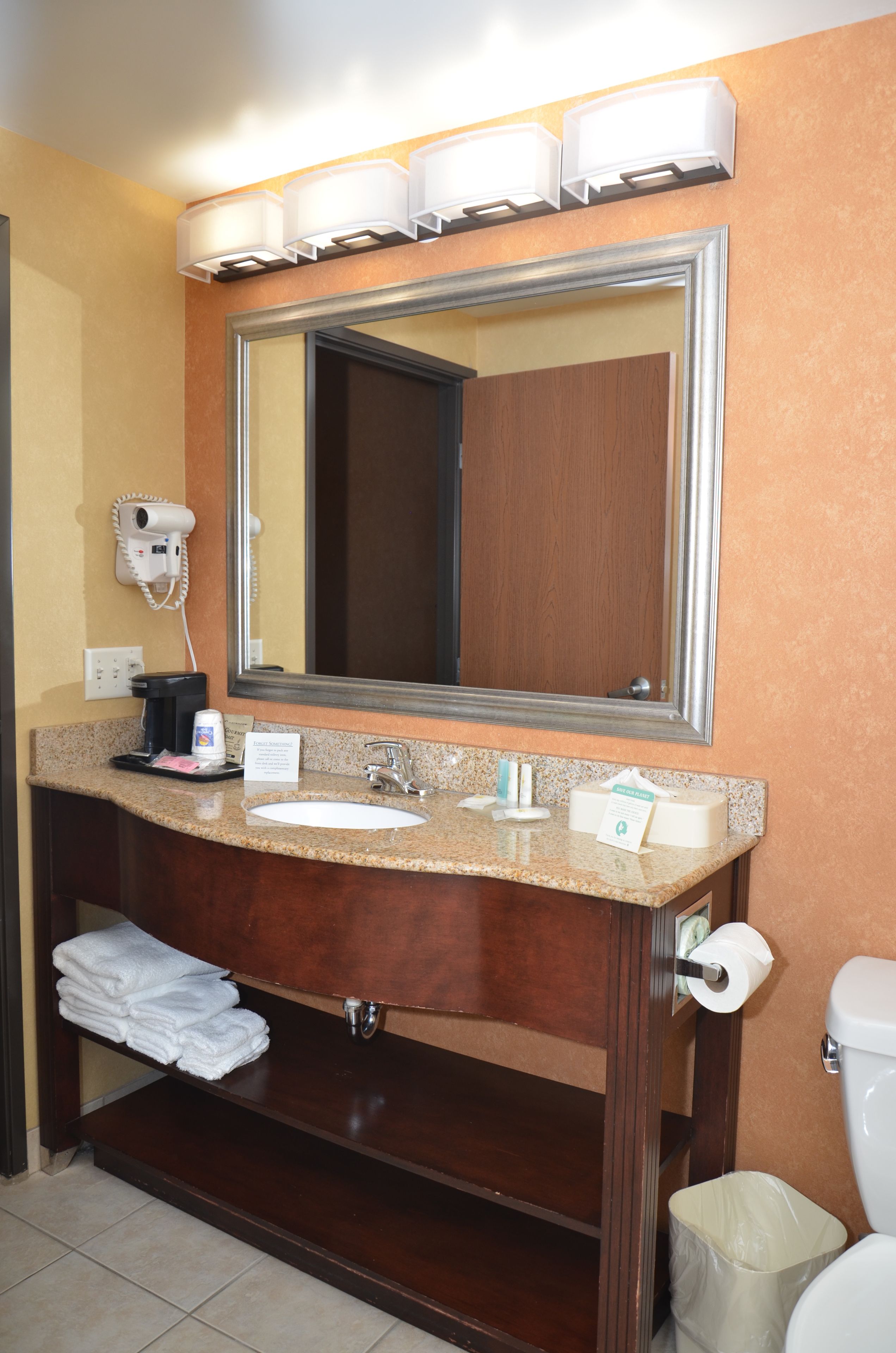 Casa de banho com lavatório, espelho, porta-toalhas e secador de cabelo na parede.