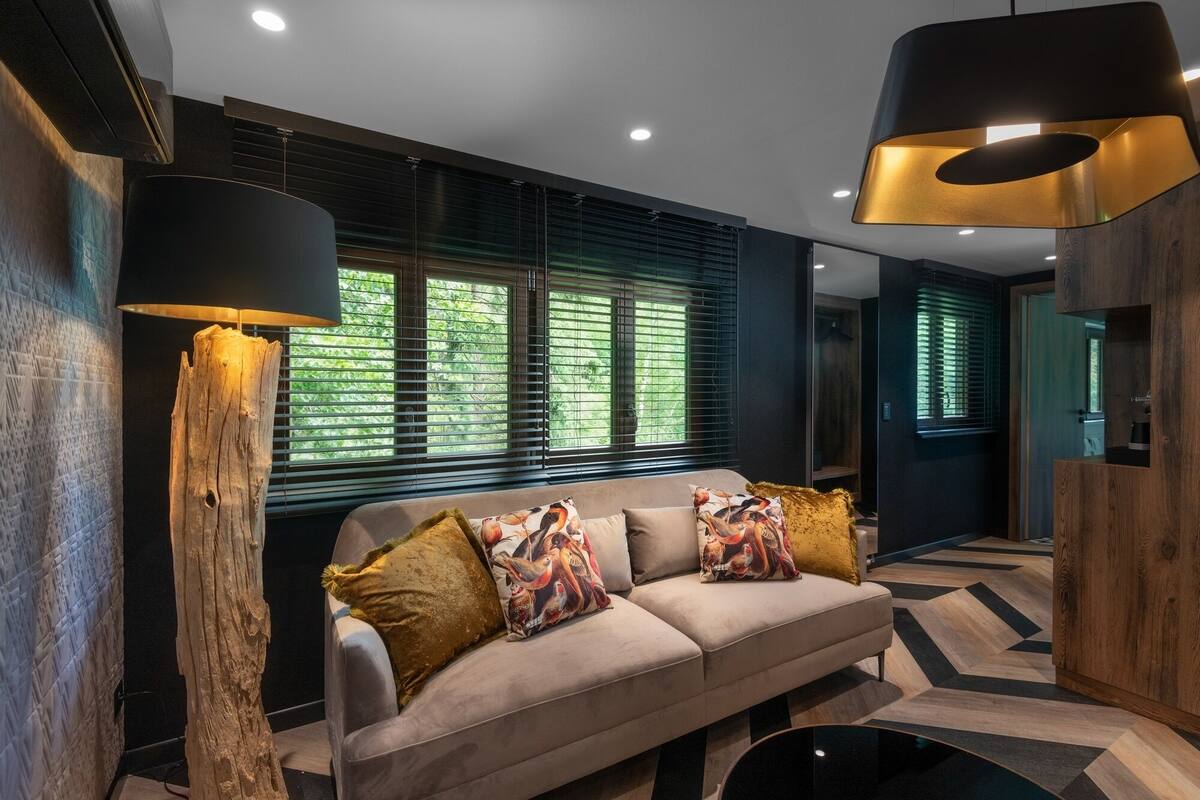 Uma sala de estar moderna com um sofá, almofadas estampadas, um candeeiro de chão de madeira alto e uma luminária pendente.