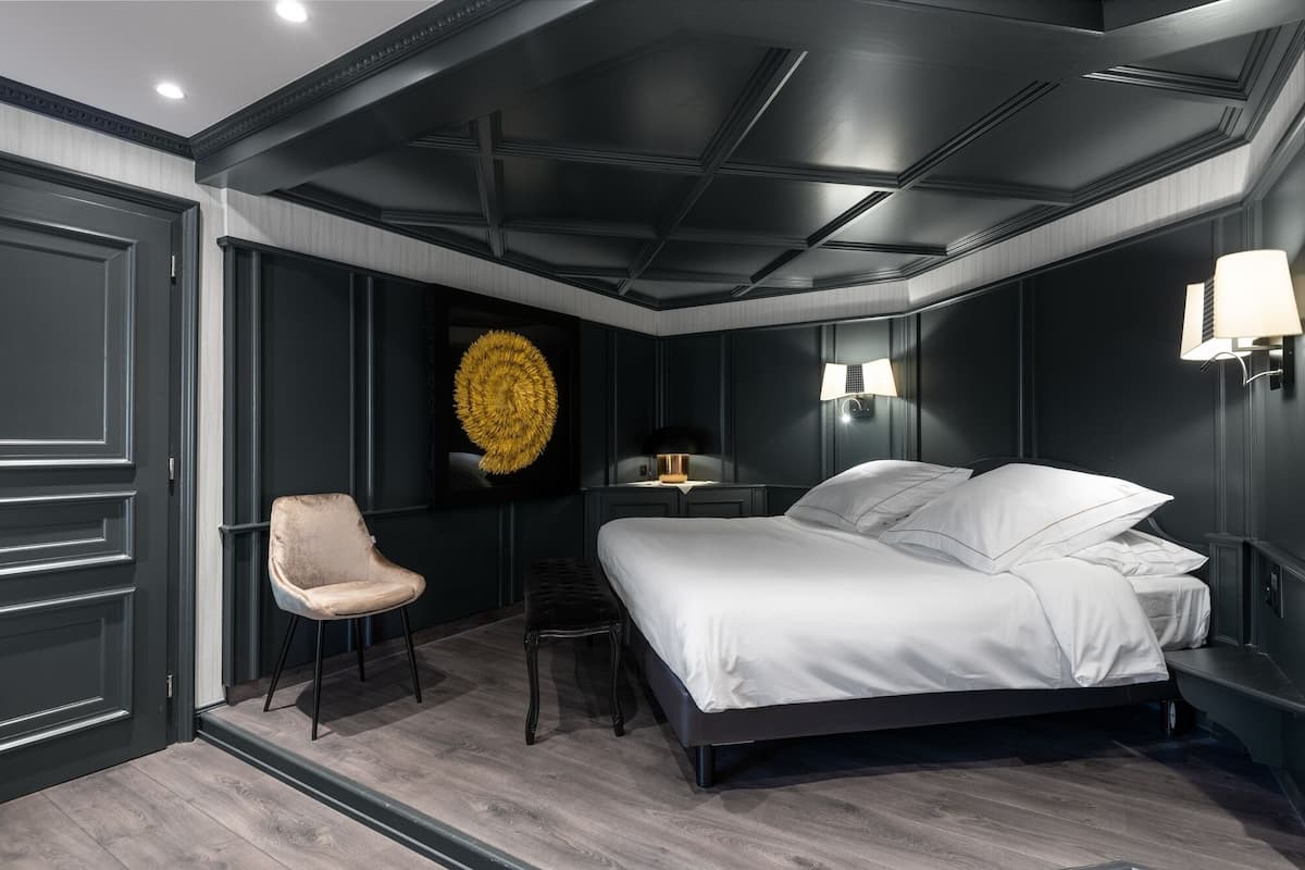 Quarto moderno com uma cama grande, uma cadeira, uma escrivaninha e um objeto decorativo na parede.