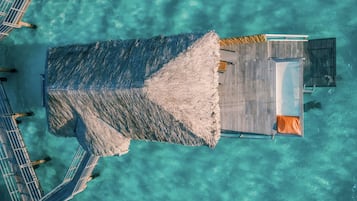 Vista aérea de um resort com um amplo deque de madeira que se estende por águas turquesa cristalinas, cercado por uma passarela de madeira.