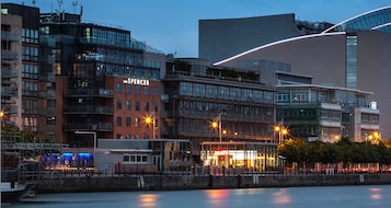 Um edifício moderno urbano com uma placa grande 'The Spencer', fachada de vidro e localização à beira-mar.