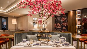Uma área de refeições com mesa posta para chá, uma árvore decorativa e um papel de parede floral.