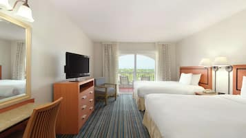 Quarto de hotel com duas camas, televisão, escrivaninha com cadeira e varanda com vista.