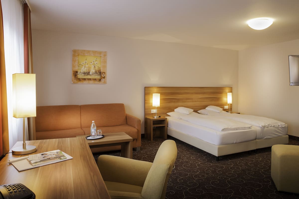 Quarto de hotel com cama, sofá, escrivaninha e cadeira.