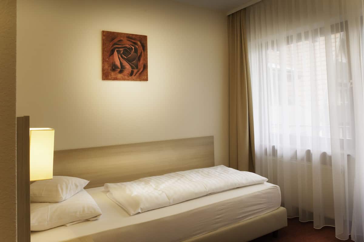 Cama bem arrumada com lençóis brancos, cabeceira de madeira e uma obra de arte na parede.