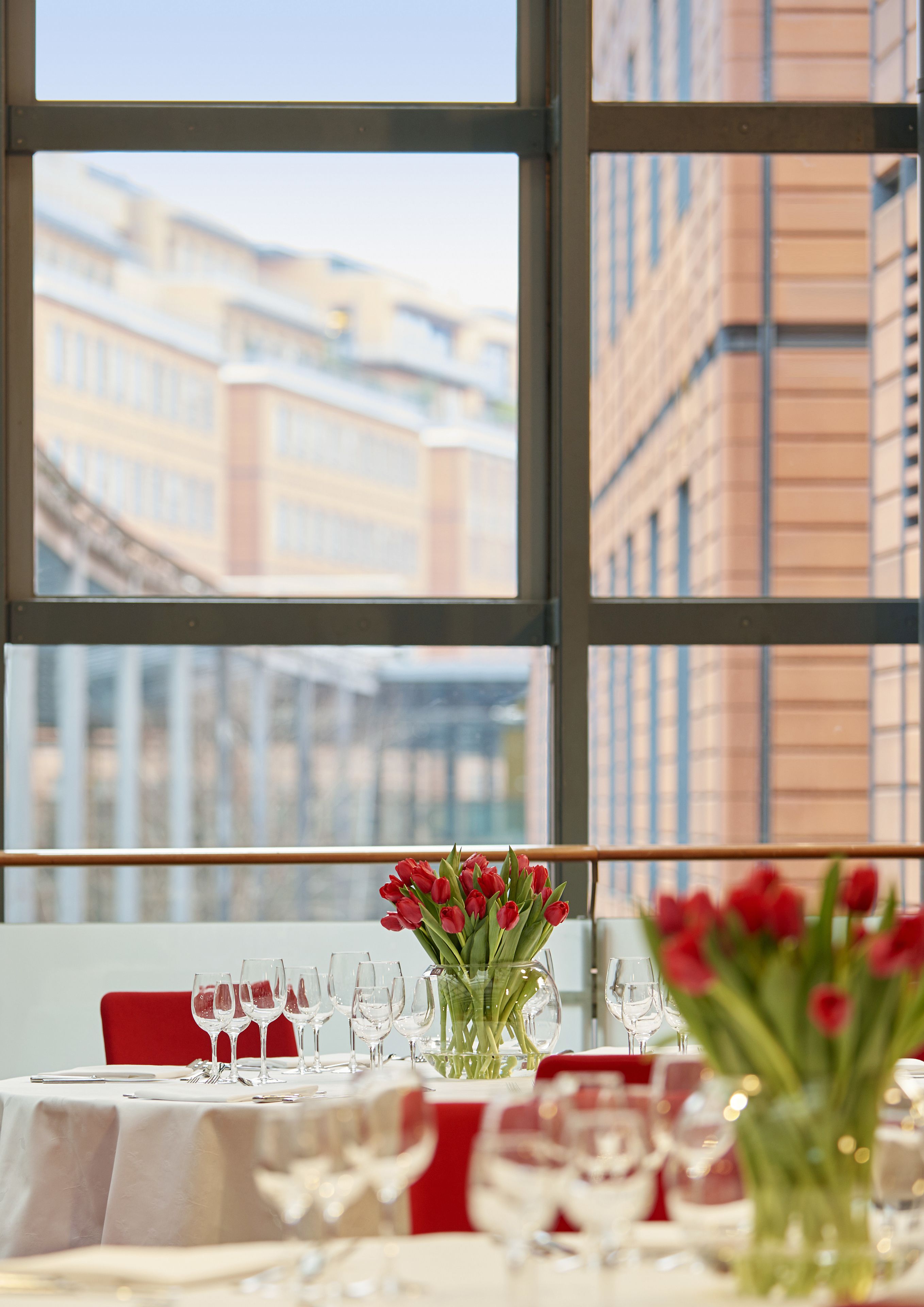 Mesa de jantar posta para quatro, com vista para prédios através de grandes janelas.