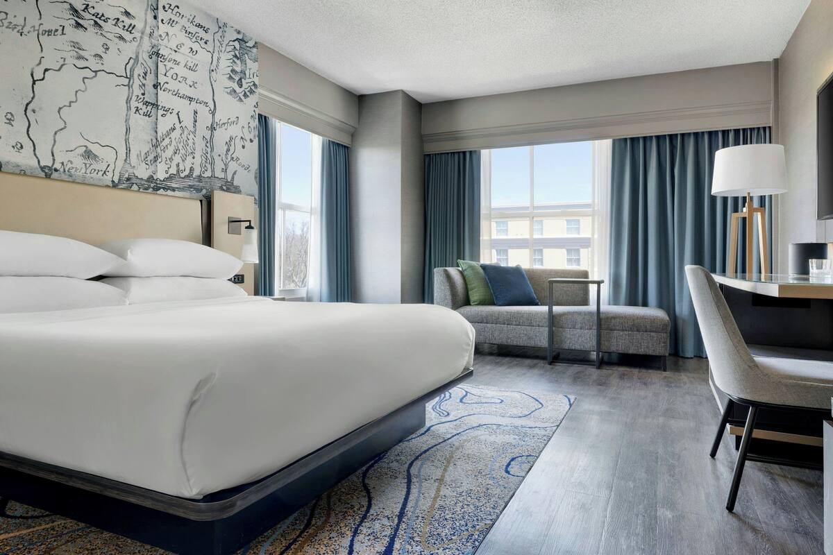 Quarto de hotel com uma cama grande, uma escrivaninha, uma cadeira e um mapa na parede.