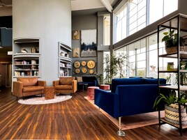 Uma sala de estar moderna com piso de madeira, poltronas de couro, um sofá azul e uma estante cheia de livros e objetos decorativos.