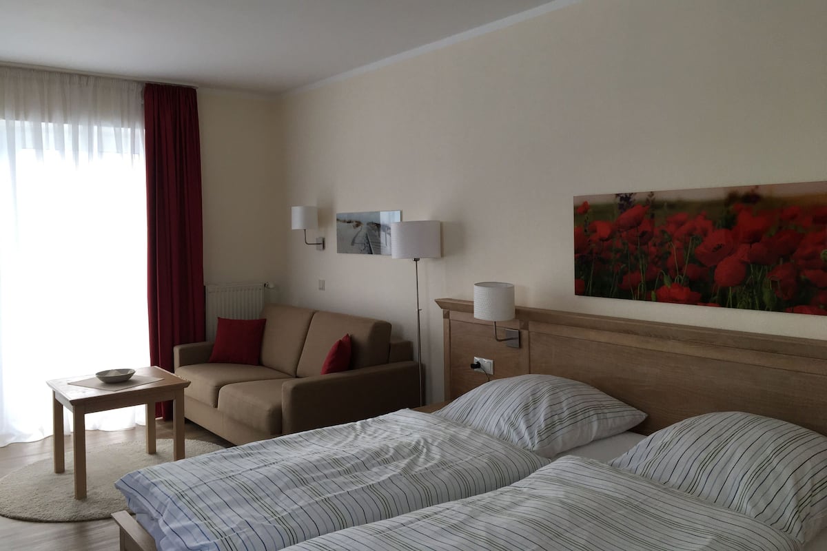 Quarto de hotel com cama, sofá, uma mesinha e um quadro na parede.