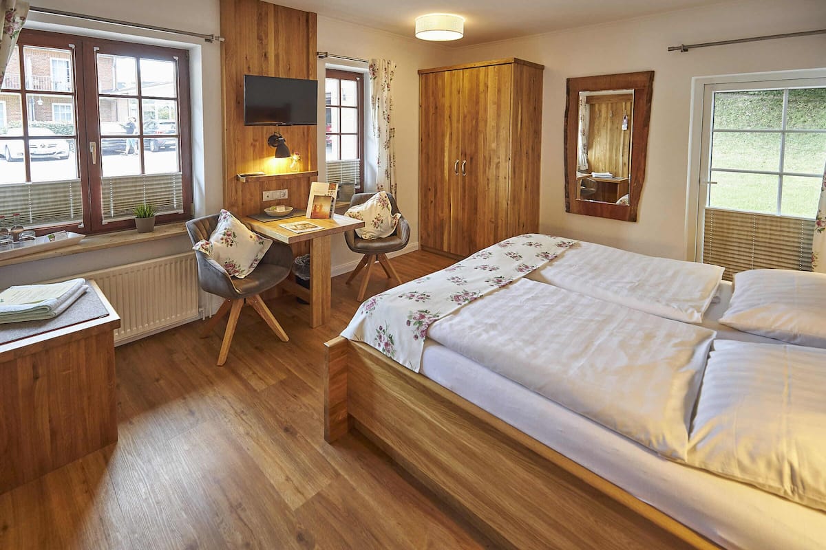 Quarto com cama de madeira, escrivaninha com cadeira, televisão e guarda-roupa.