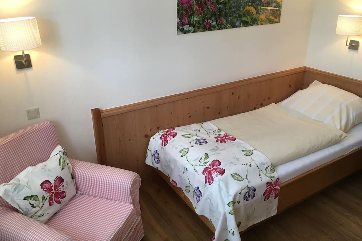 Uma cama de solteiro com colcha florida, cabeceira de madeira e duas luminárias de apoio.