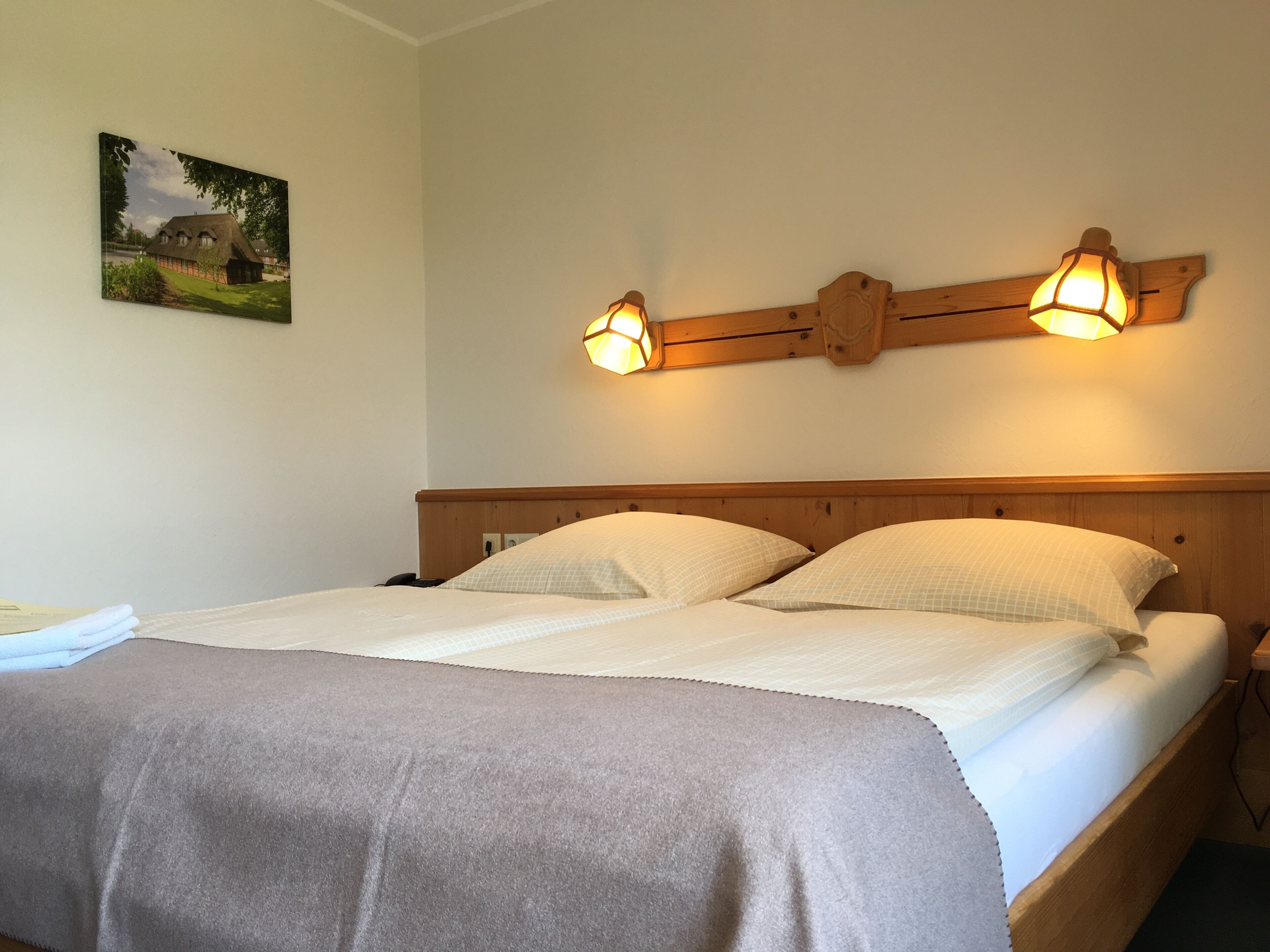 Uma cama bem arrumada com cabeceira de madeira, duas luminárias de apoio e um quadro na parede.