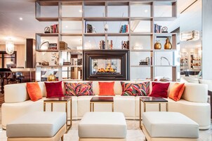 Uma sala de estar moderna com um sofá branco, almofadas coloridas, uma lareira e uma estante repleta de livros e objetos decorativos.
