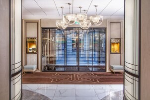Um hall com um lustre moderno, portas de vidro e piso de mármore.