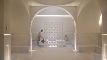 Um hall de hotel moderno com uma grande porta em arco, parede estampada e uma pessoa caminhando em direção a uma área de estar.