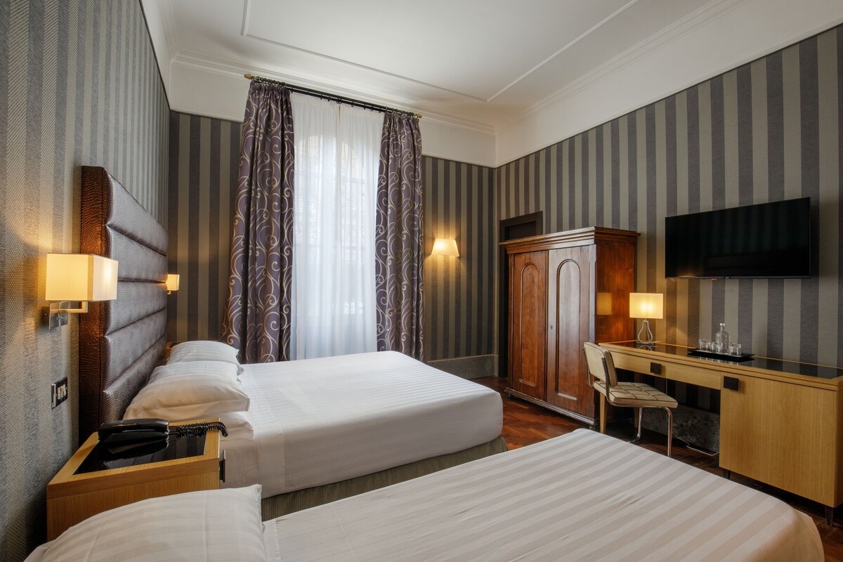 Quarto de hotel com duas camas, uma escrivaninha, televisão e armário.