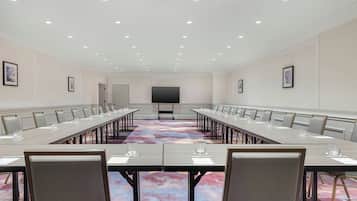 Uma sala de conferências com mesas compridas, cadeiras, um grande ecrã e quadros nas paredes.