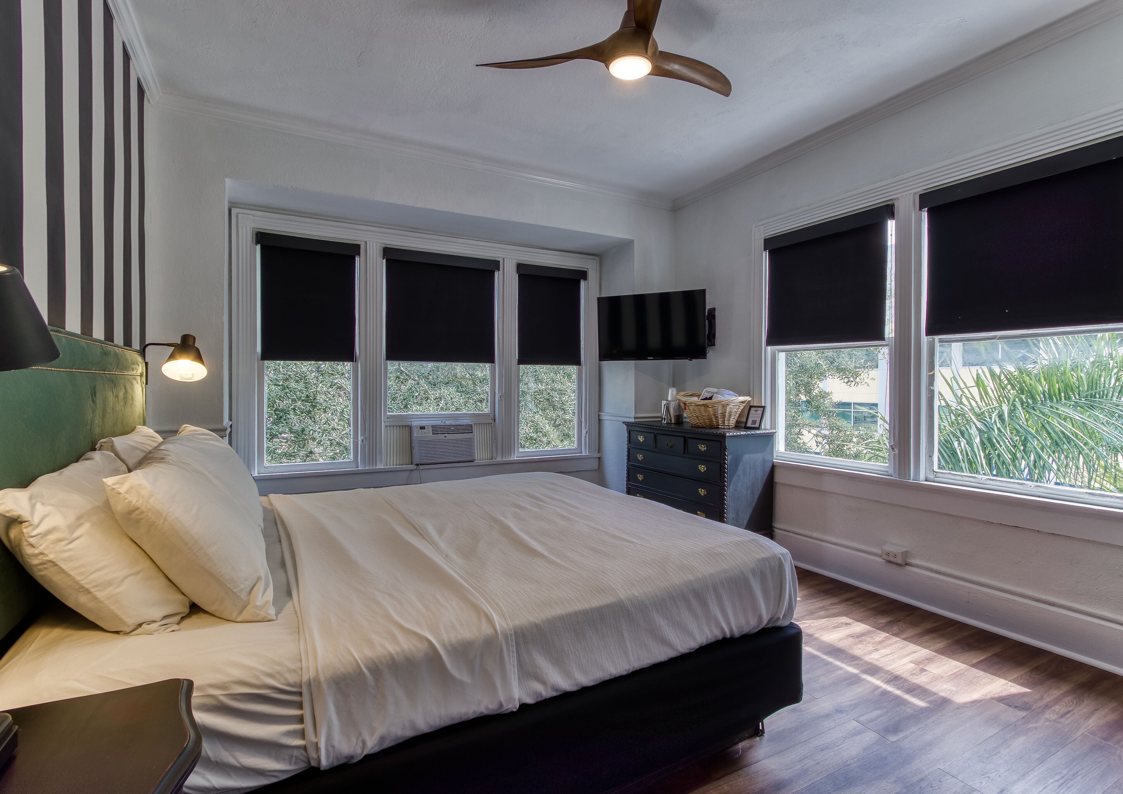 Um quarto com cama, cômoda, televisão e ventilador de teto.