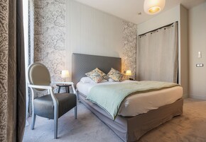 Quarto com cama, poltrona, mesa de cabeceira e parede com padrão floral.