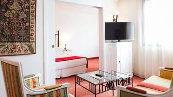 Quarto de hotel com cama, televisão, mesa de centro de vidro e uma cadeira.