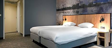Quarto de hotel com uma cama grande, cabeceira com arte na parede, mesa de cabeceira e porta que dá para outro cômodo.