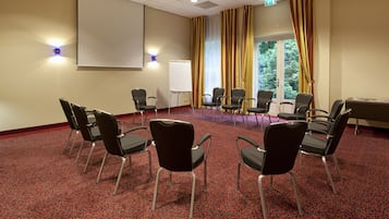 Uma sala de conferências com carpete vermelho, cadeiras pretas, lousa branca e tela de projetor.