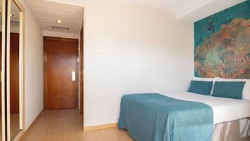 Quarto de hotel com uma cama, um cobreleito verde-água, um quadro abstrato grande na parede e uma porta de madeira.