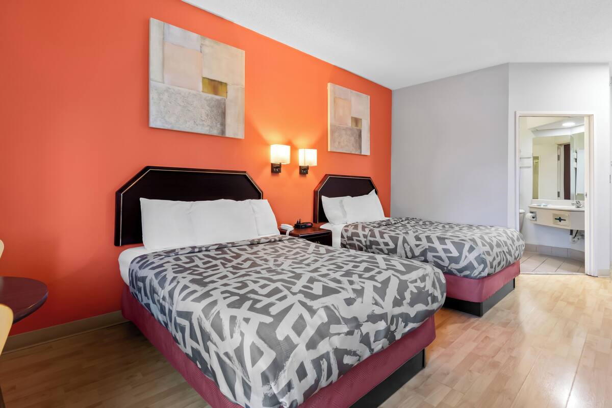 Quarto de hotel com duas camas, paredes alaranjadas e chão de madeira.