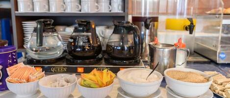 Disposição de buffet com máquinas de café, recipientes com comida e um espaço para café.