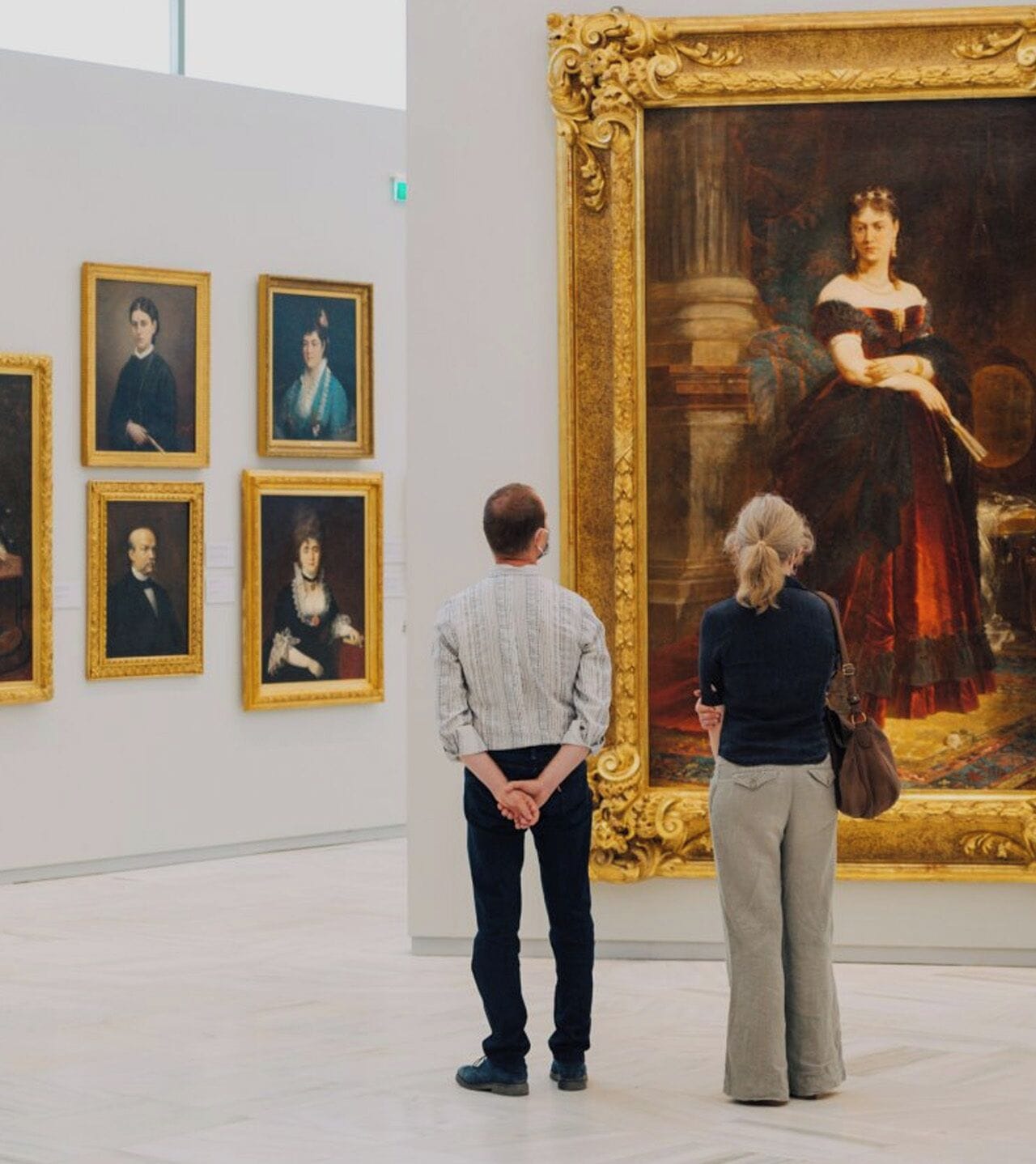 Uma galeria com retratos emoldurados na parede e uma pintura grande em primeiro plano.