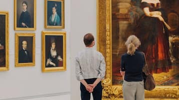 Uma galeria com retratos emoldurados na parede e uma pintura grande em primeiro plano.
