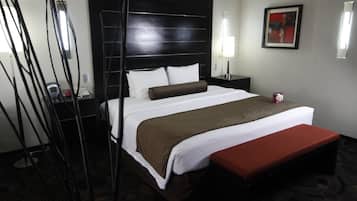 Quarto de hotel com uma cama grande, mesa de cabeceira com abajur, telefone ao lado da cama e um quadro na parede.