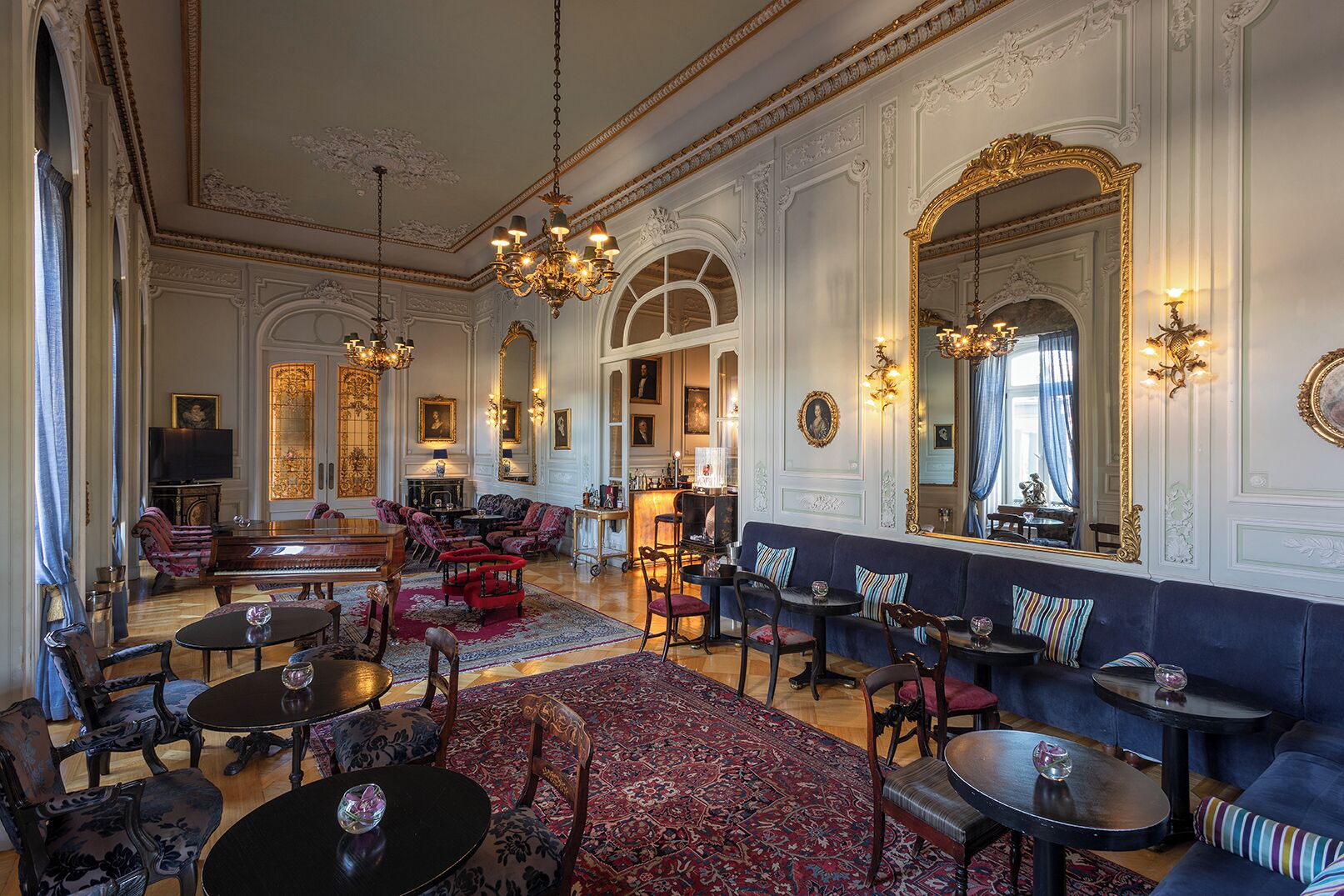 Um hall de hotel luxuoso com decoração requintada, um lustre imponente e uma área de estar com sofás e mesas.