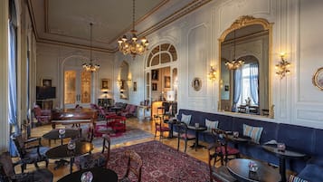 Um hall de hotel luxuoso com decoração requintada, um lustre imponente e uma área de estar com sofás e mesas.