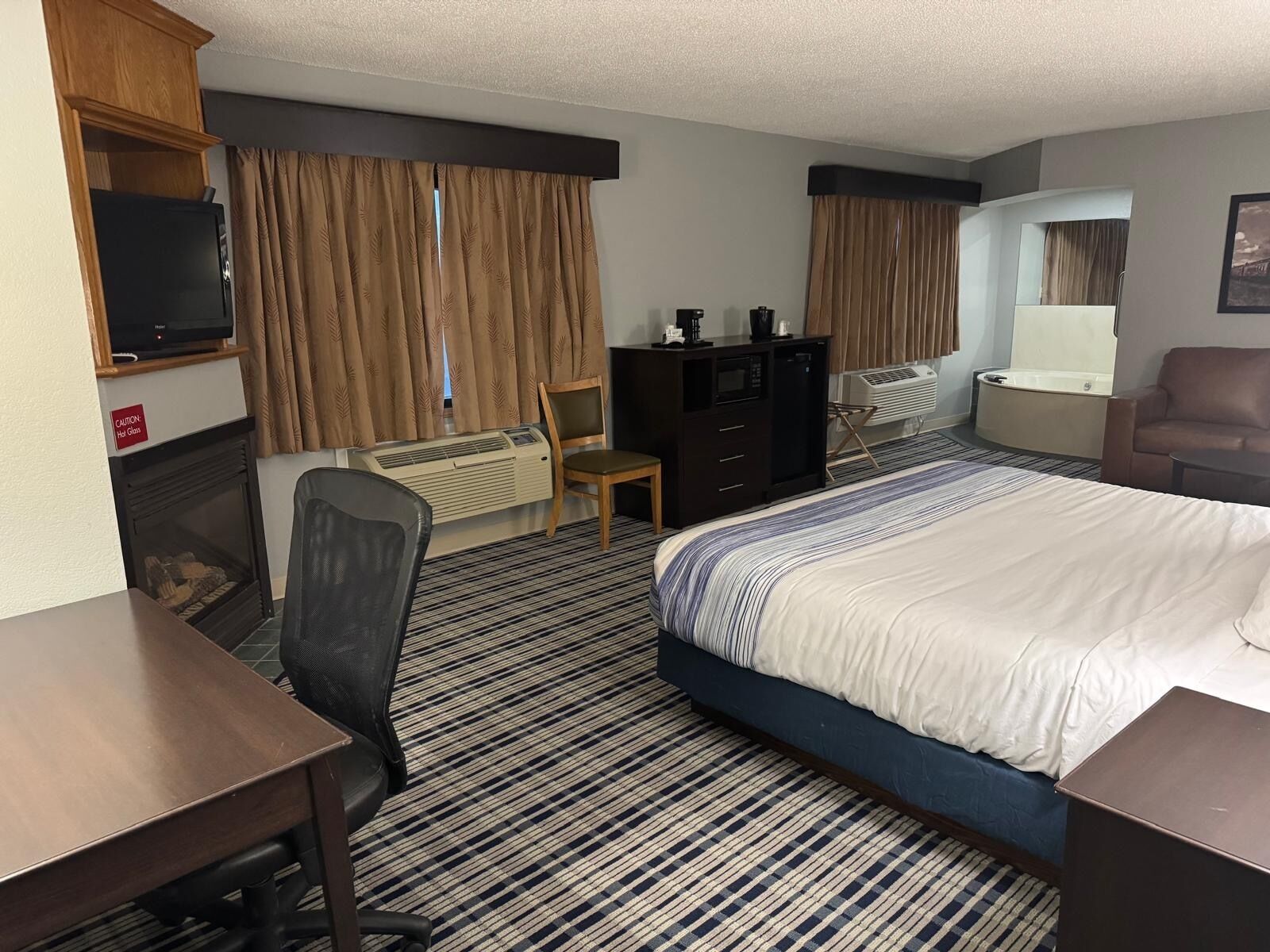 Quarto de hotel com cama, escrivaninha, cadeira, televisão, aquecedor e banheira.