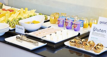 Buffet com diversas opções de comida, incluindo frutas, iogurte e alternativas sem glúten.