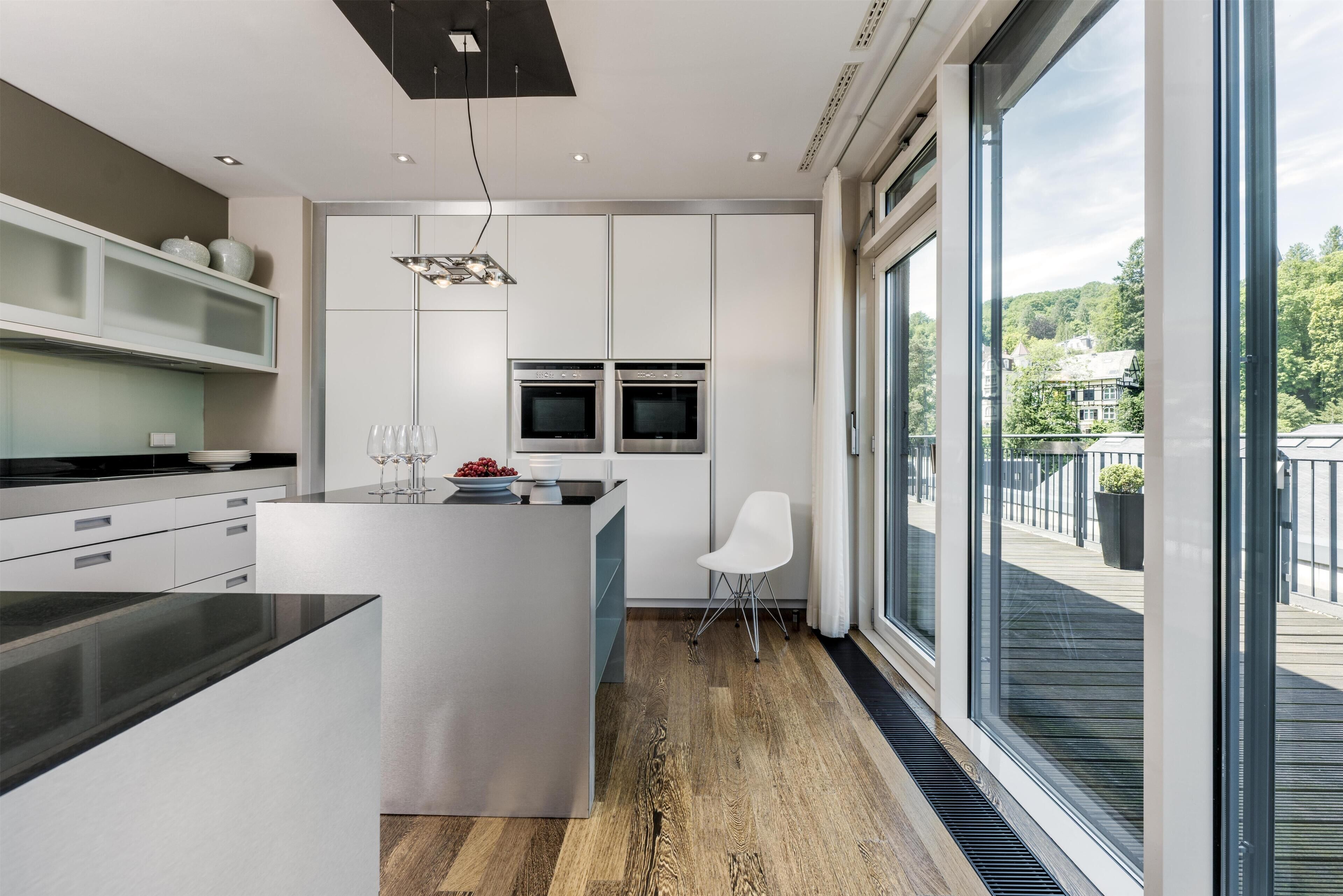Cozinha moderna com ilha central, eletrodomésticos embutidos e vista para uma varanda.