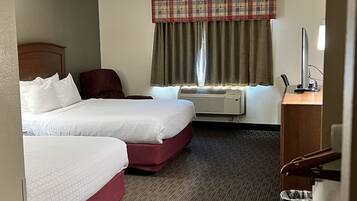 Quarto de hotel com duas camas, uma mesa, uma cadeira, janela com cortinas e ar condicionado fixado na parede.