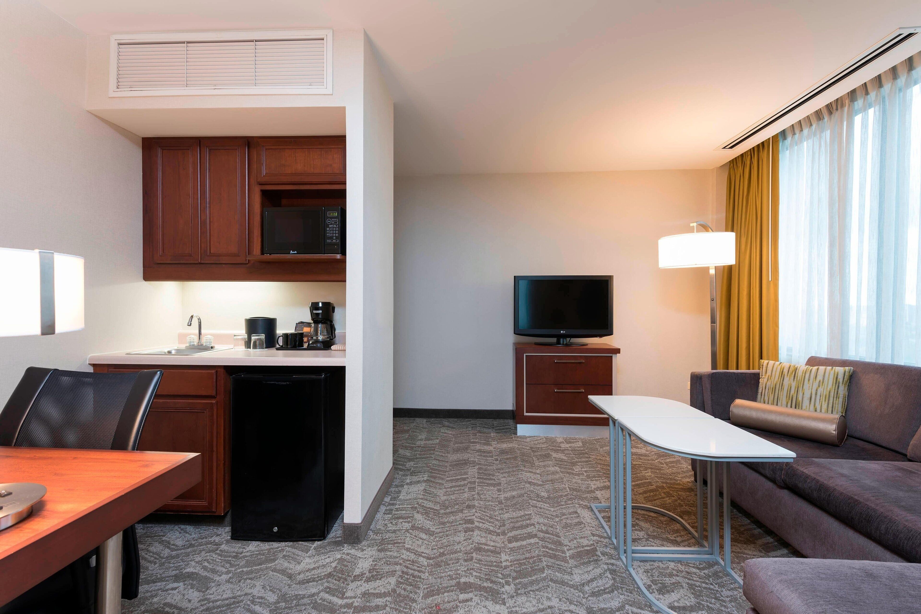 Quarto de hotel com cozinha compacta, televisão de tela plana, sofá e mesa de jantar.