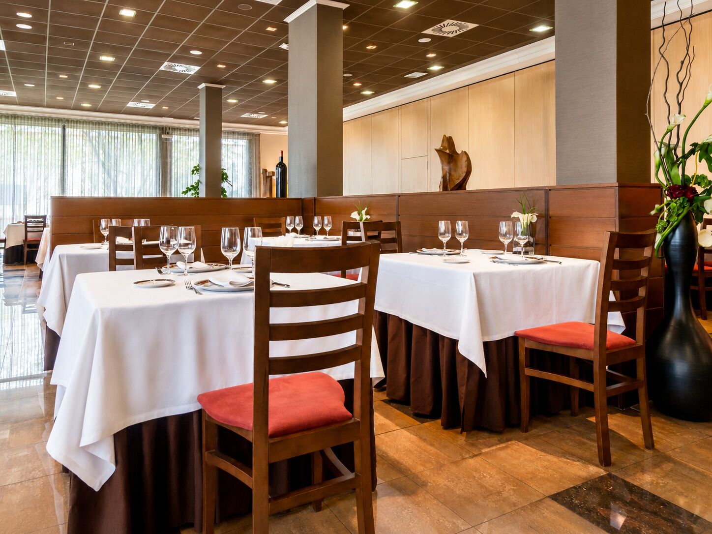 Restaurante com várias mesas, cada uma com toalhas brancas e cadeiras de madeira.
