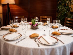 Uma mesa de jantar redonda posta com pratos, talheres, copos e doces, com um vaso de flores no centro.