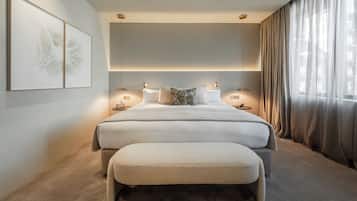 Quarto moderno com cama grande, abajures, cabeceira com linhas verticais, um banco aos pés da cama e uma janela com cortinas.