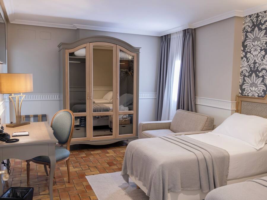 Quarto de hotel com cama, escrivaninha com cadeira, guarda-roupa e janela com cortinas.