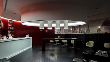Uma área de bar moderna com um balcão de recepção curvo, vários banquetes e um grande candelabro.