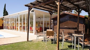 Um espaço de varanda exterior moderno com estrutura de vidro, mesas e cadeiras de madeira.