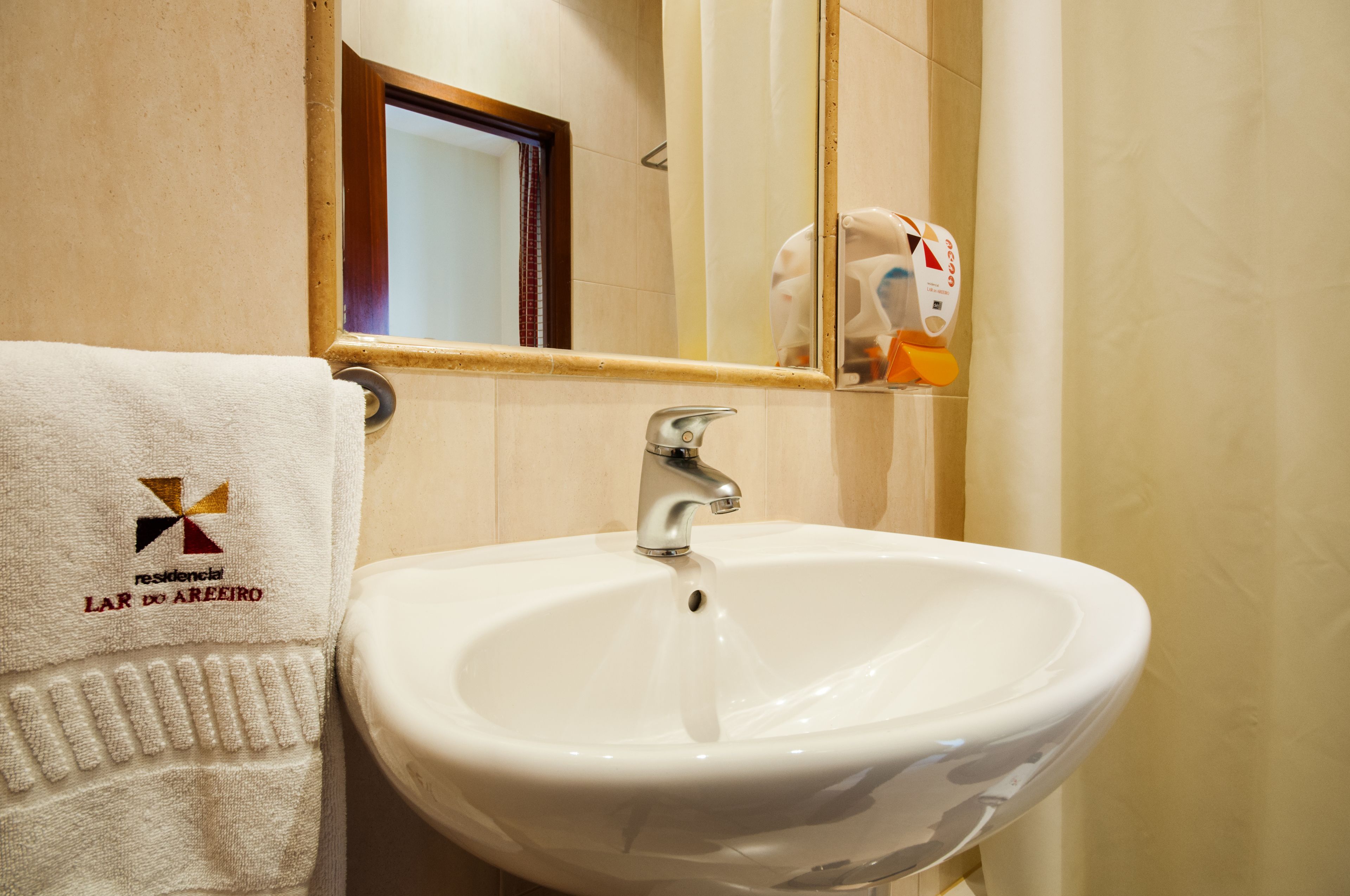 Um banheiro com pia branca, uma toalha com logotipo e um espelho sobre a pia.