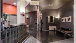 Um hall moderno com uma receção, um banco, um pilar grande e um quadro de informações fixado na parede.