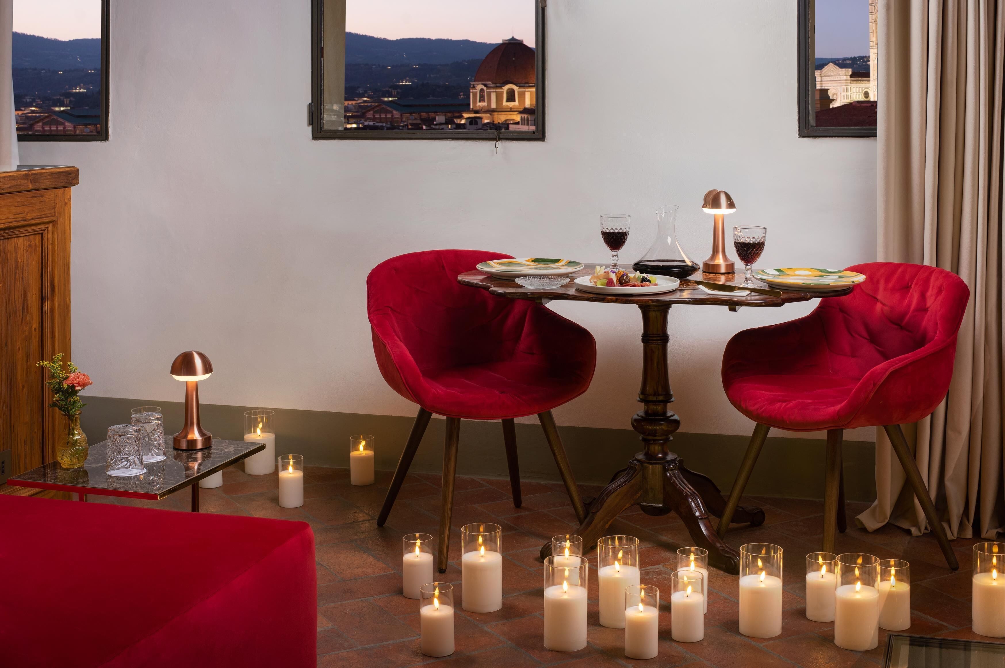 Uma área de jantar com mesa posta para dois, rodeada por velas, e vistas da cidade emolduradas nas paredes.