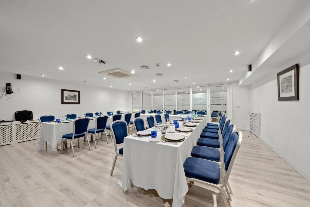 Sala de conferências com várias mesas e cadeiras, paredes brancas e luminárias no teto.